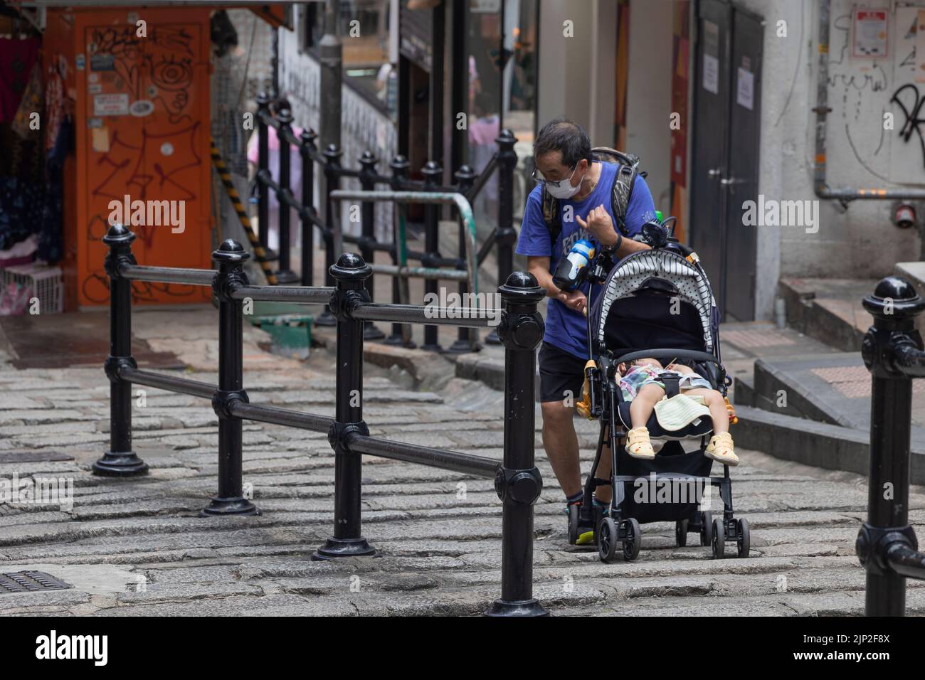 A man in a mask pulling a stroller with a baby on the street in Hong ...