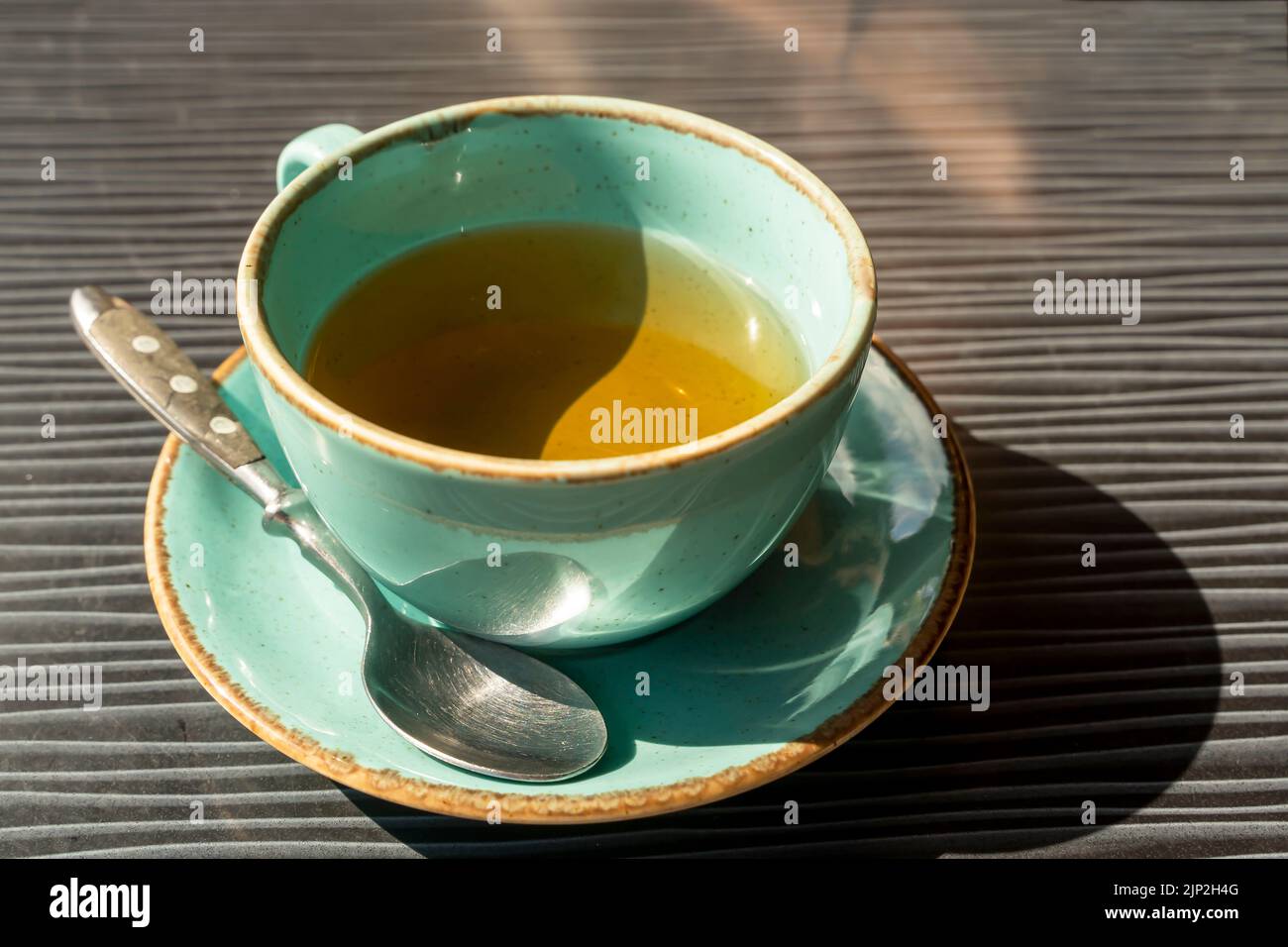 unfinished turquoise cup of tea on a table in a cafe in the sunlight ...