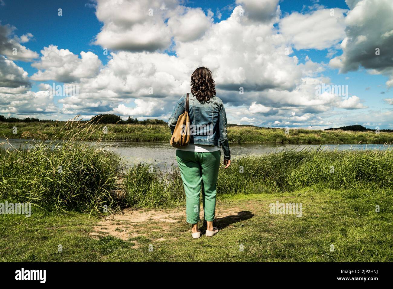 woman stands on the bank of a small river and looks into the distance ...