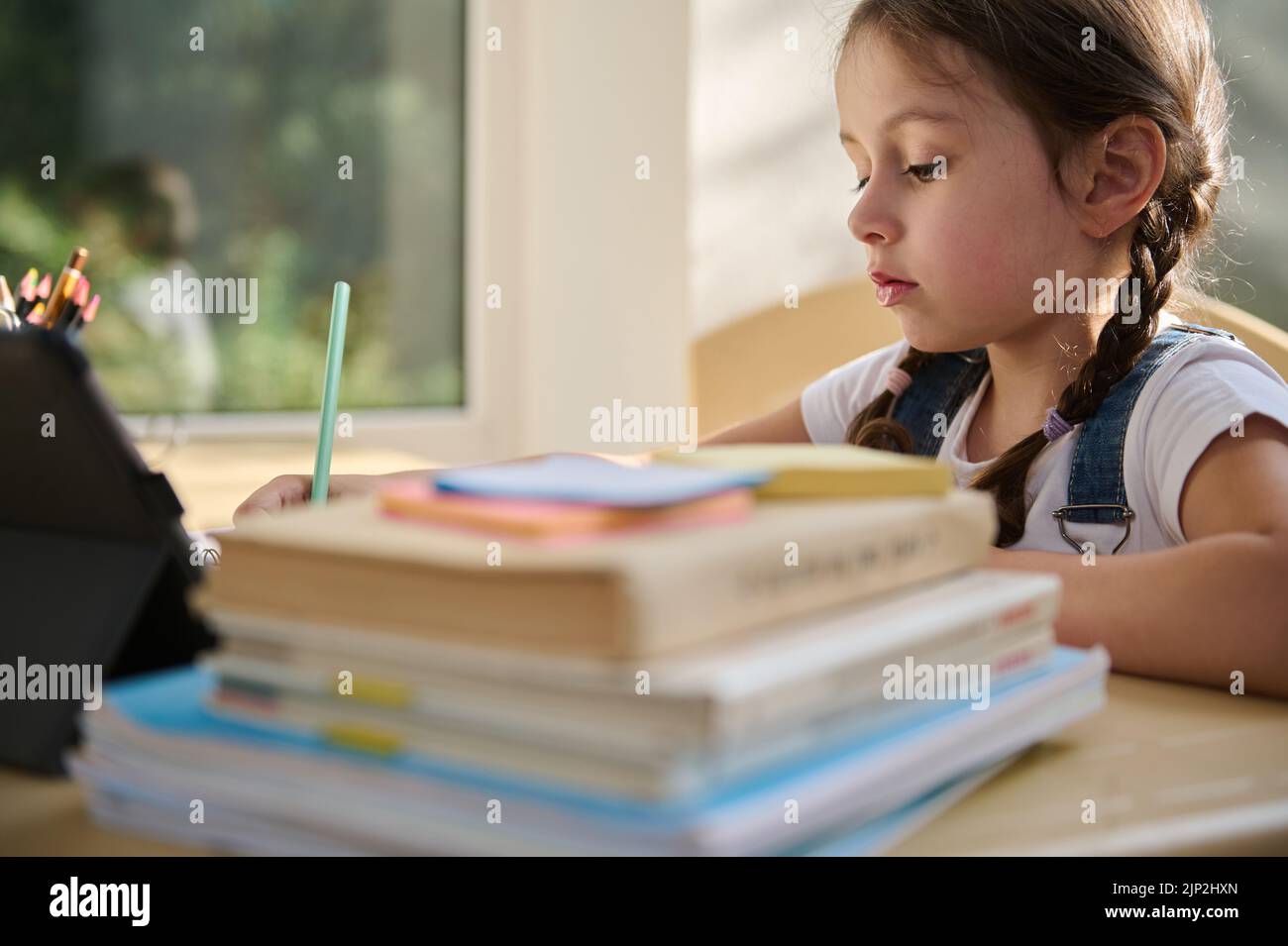 Adorable schoolgirl doing homework with digital tablet at home ...