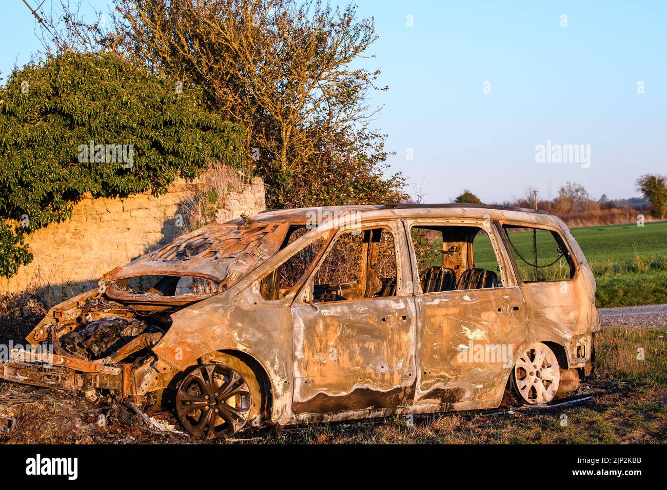 An old abandoned ruined car in a field near an asphalt road Stock Photo ...