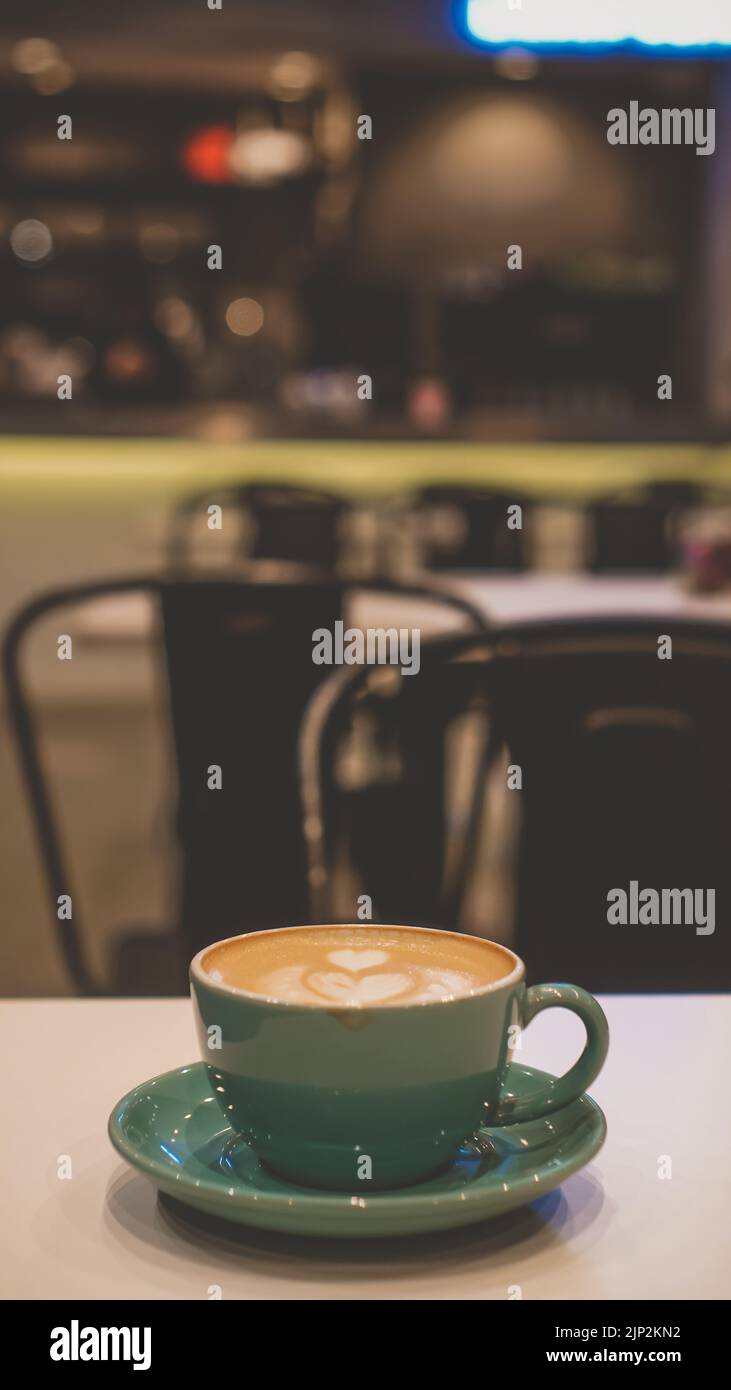 A vertical shallow focus of a mug of coffee with heart shapes on it ...