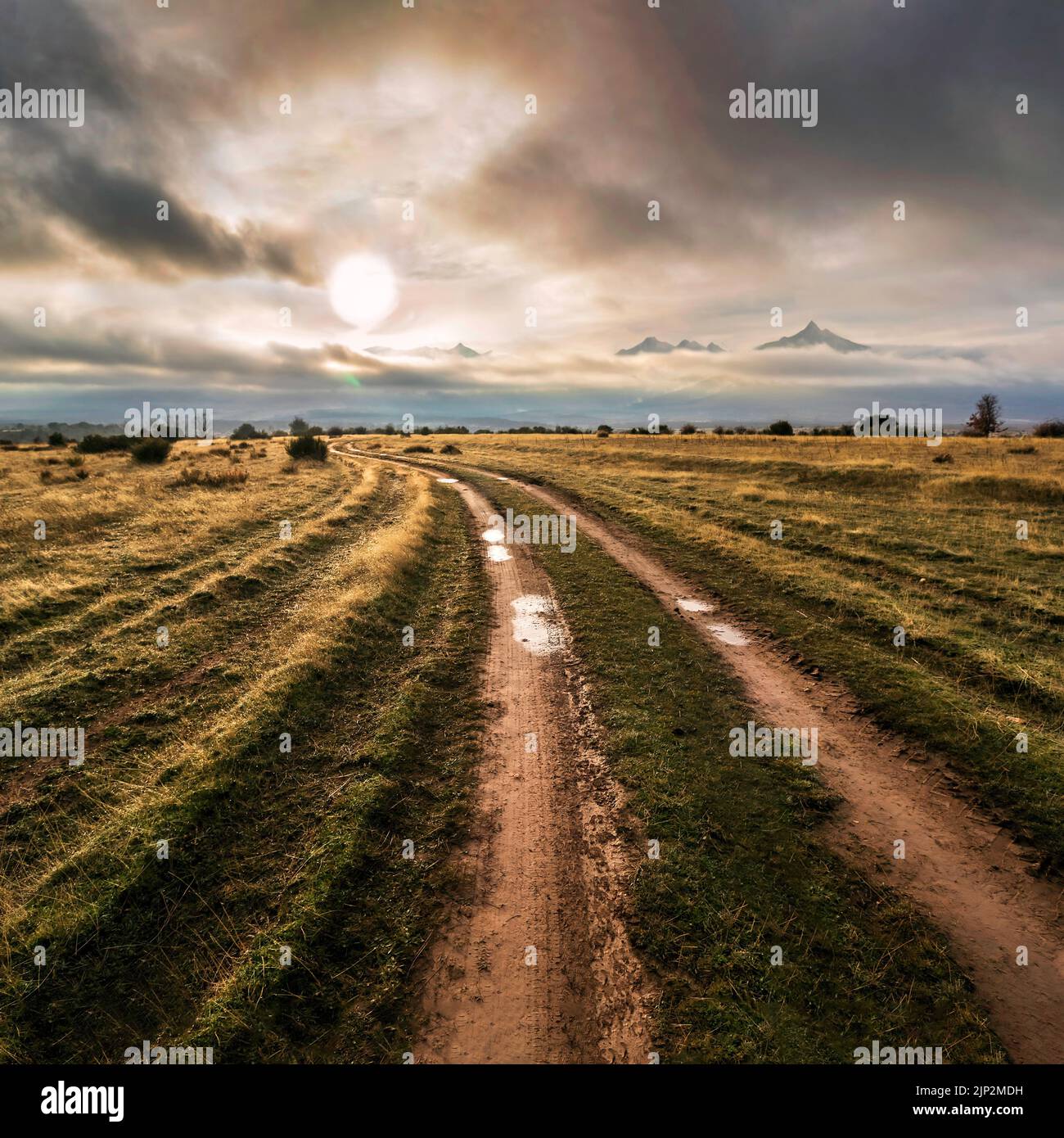 Dirt road landscape towards mountains with sun on the horizon, dark ...