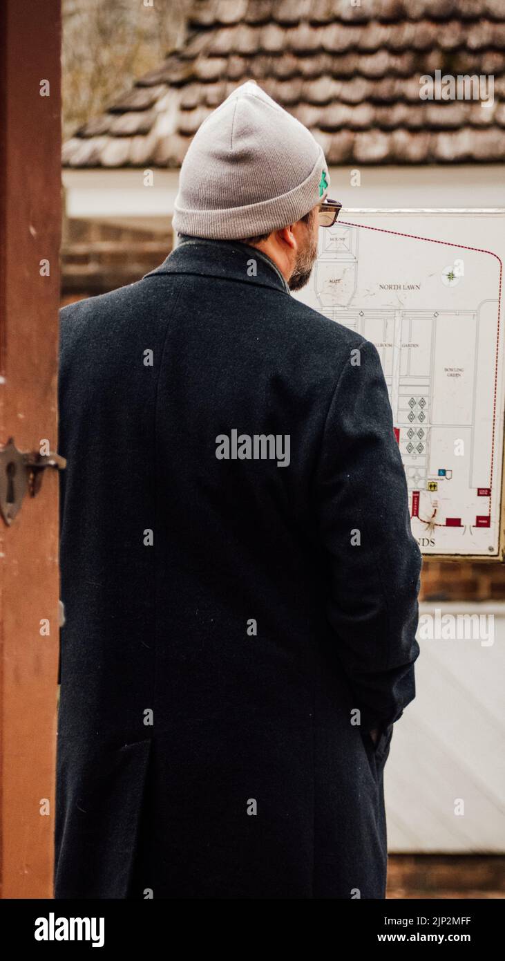A vertical back view of an adult man in a black coat and white hat ...