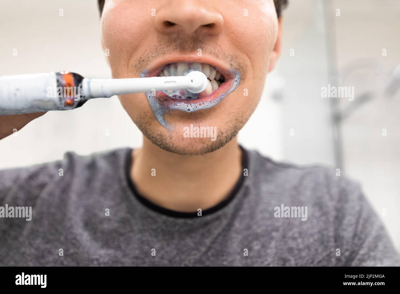 A closeup of young man with electrical toothbrush brush his teeth with ...