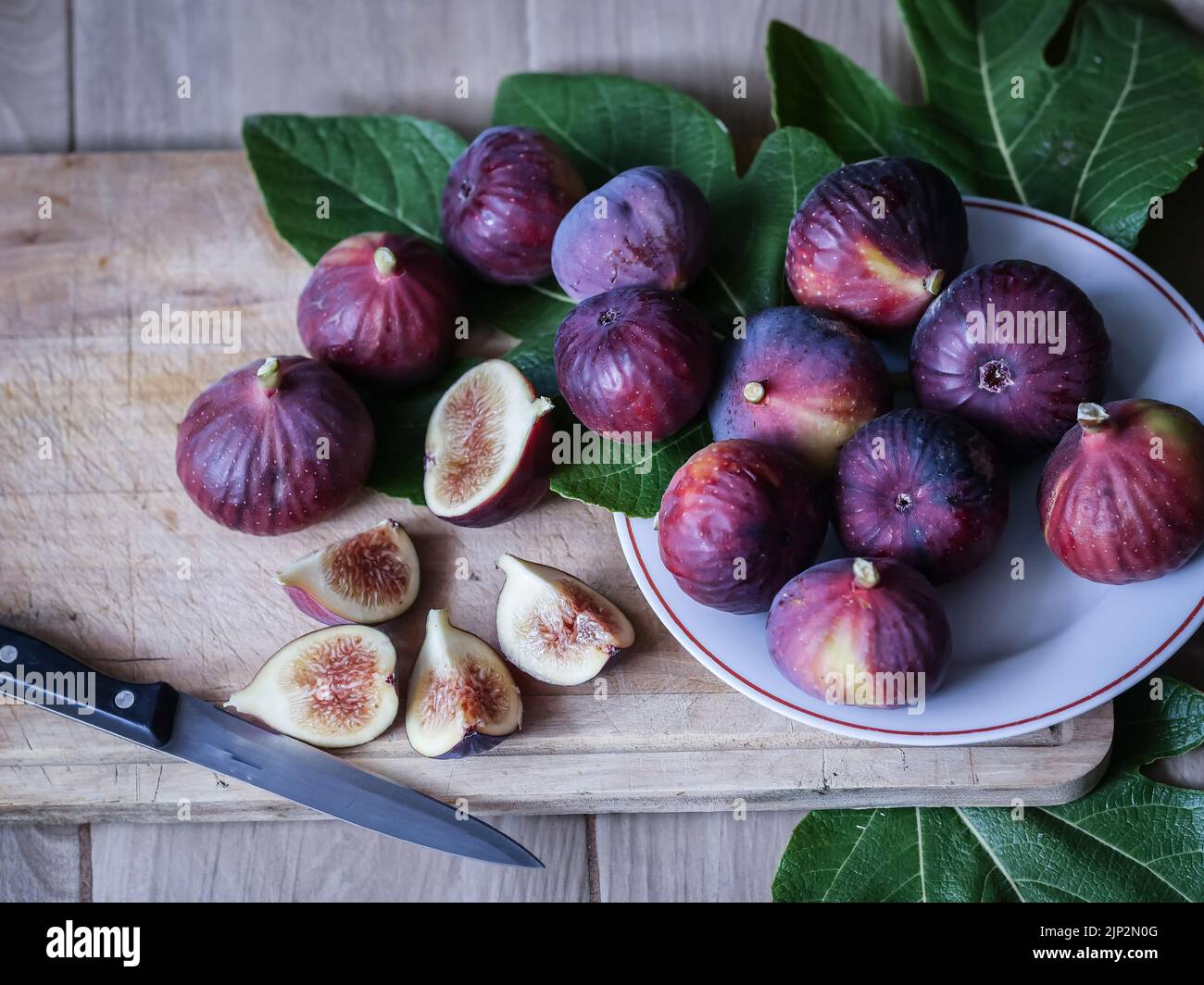 A top view of a plate full of figs on a cutting board with cut figs in ...