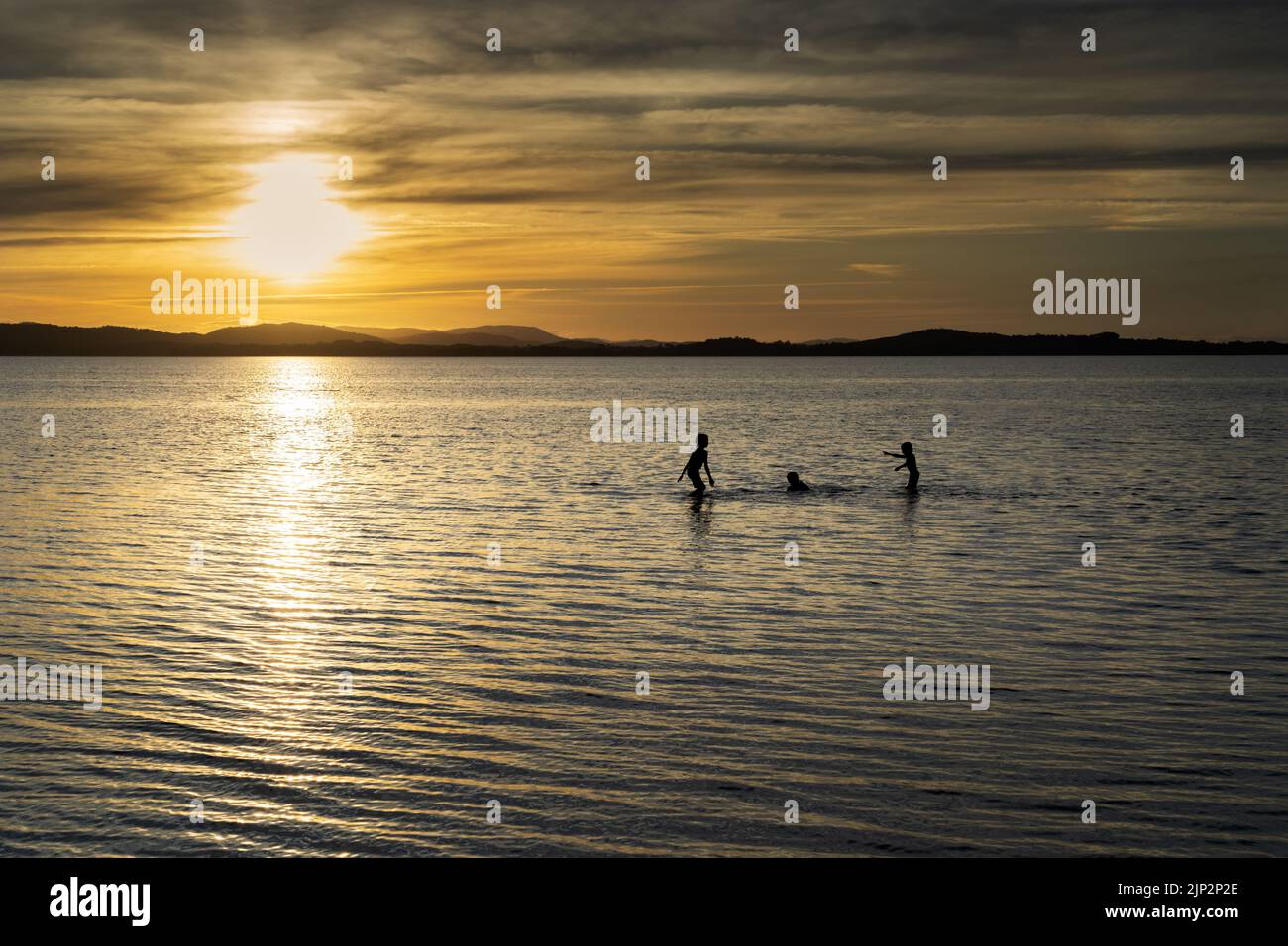 A beautiful sunset over Wallis Lake with silhouettes of kids playing in ...