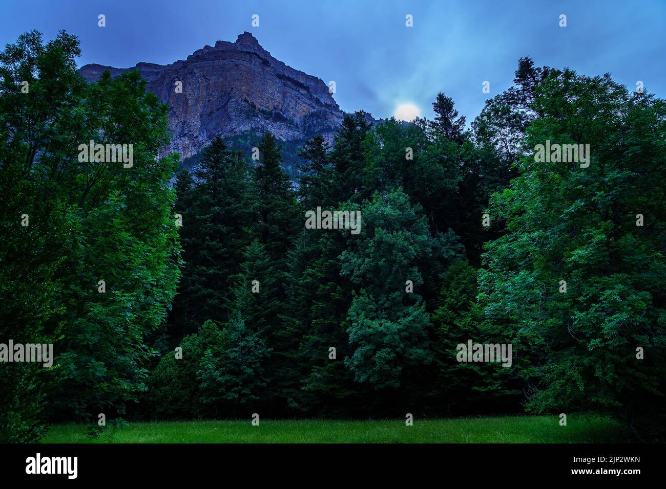Dark landscape with mountain, sun or moon, green grass trees. Ordesa ...