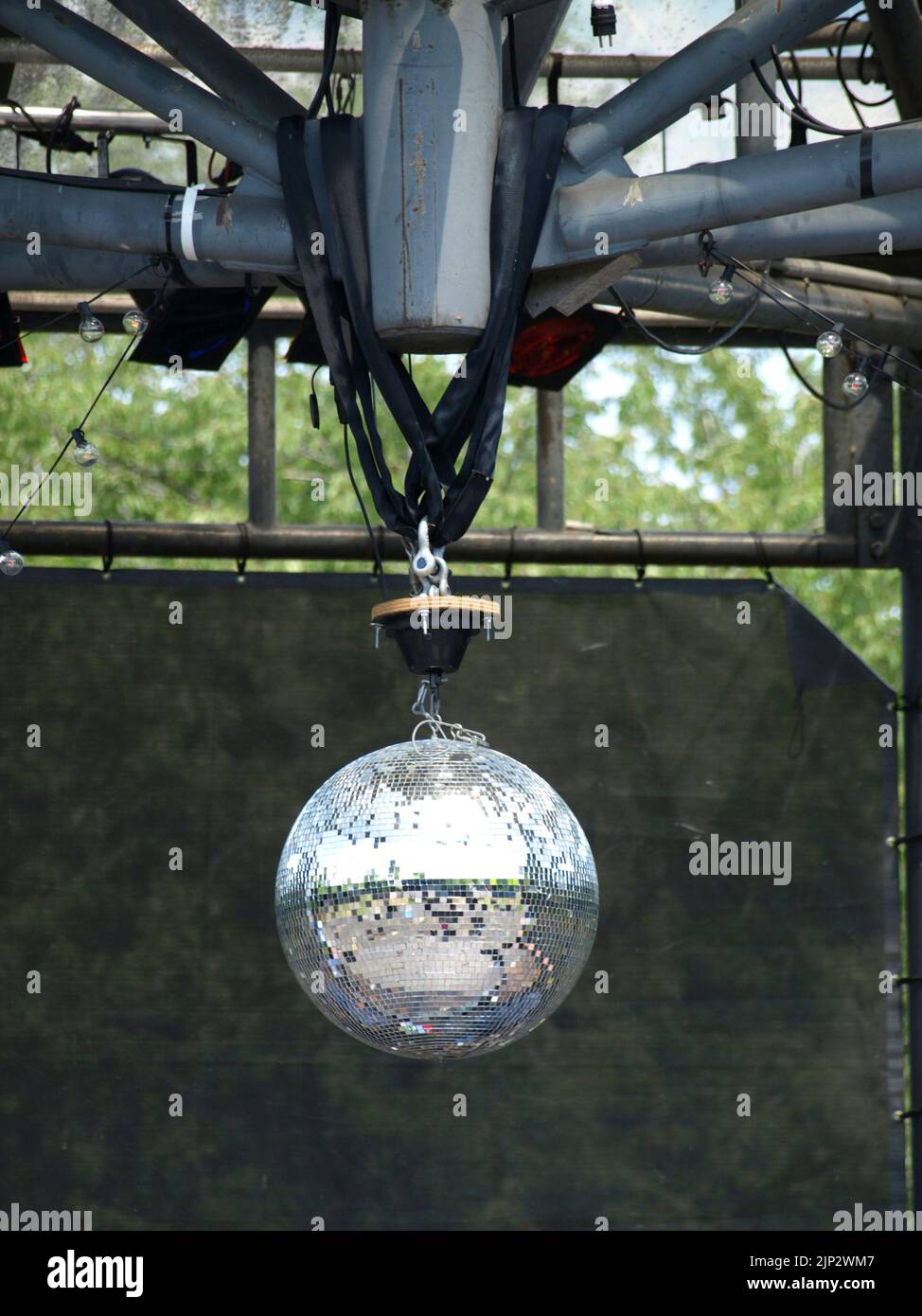 A mirror disco ball hangs over an outdoor stage. Sunny weather. No ...