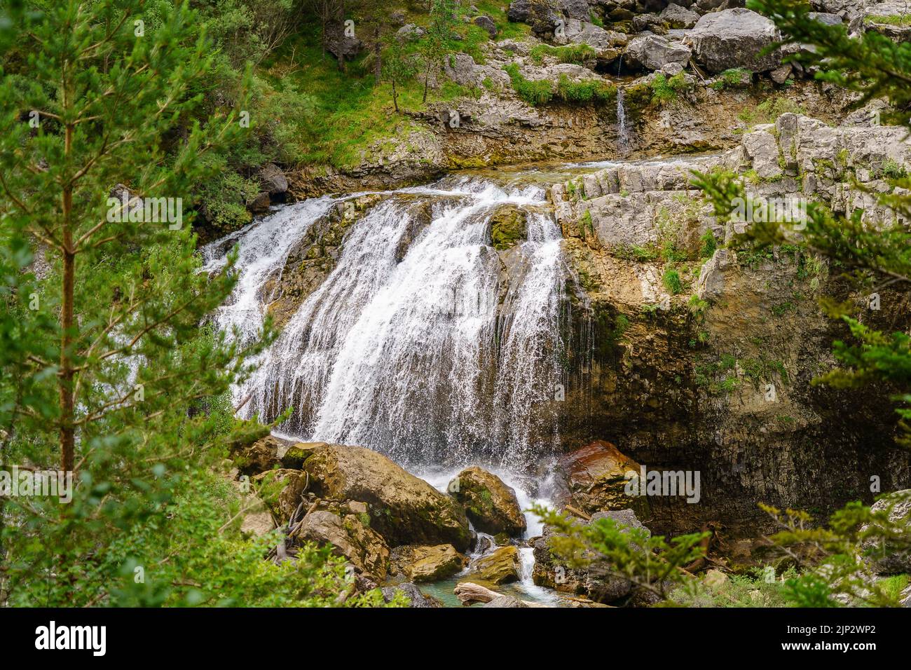 Waterfall in the green forest with rocks and pine trees framing the ...