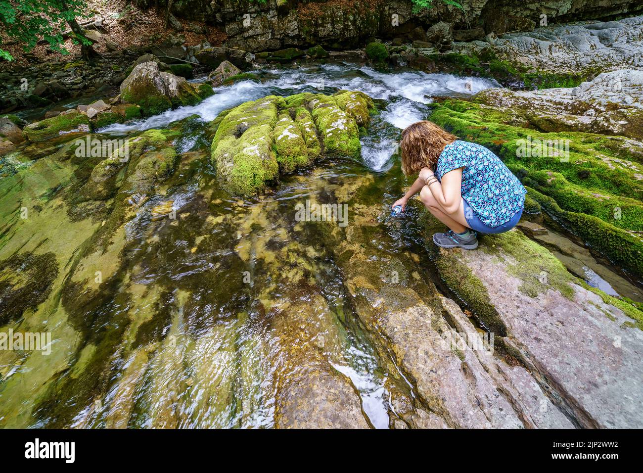 Woman catching water from a clean water river in the mountains. Beauty ...