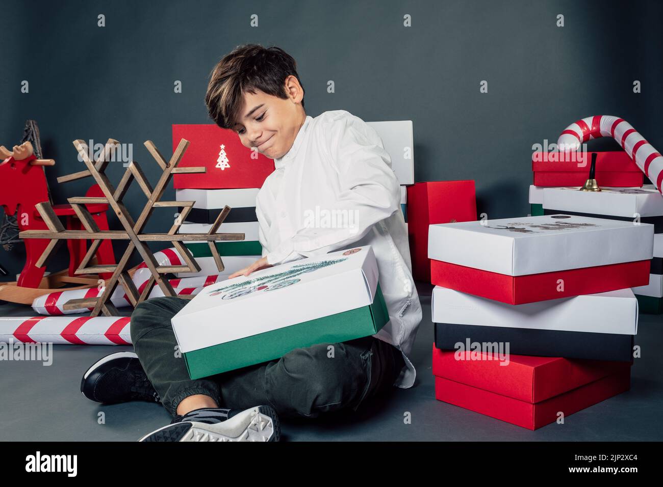 A handsome teen boy sit on floor in front of Christmas boxes tower and ...