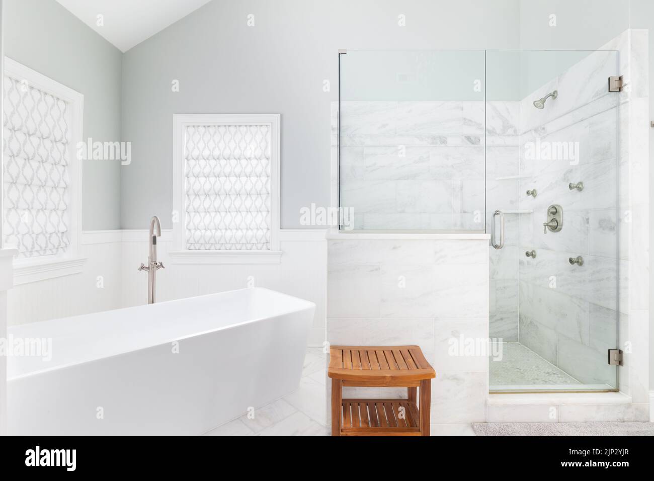 A luxury bathroom with a standalone tub and walk-in shower lined with glass and marble tiles ...