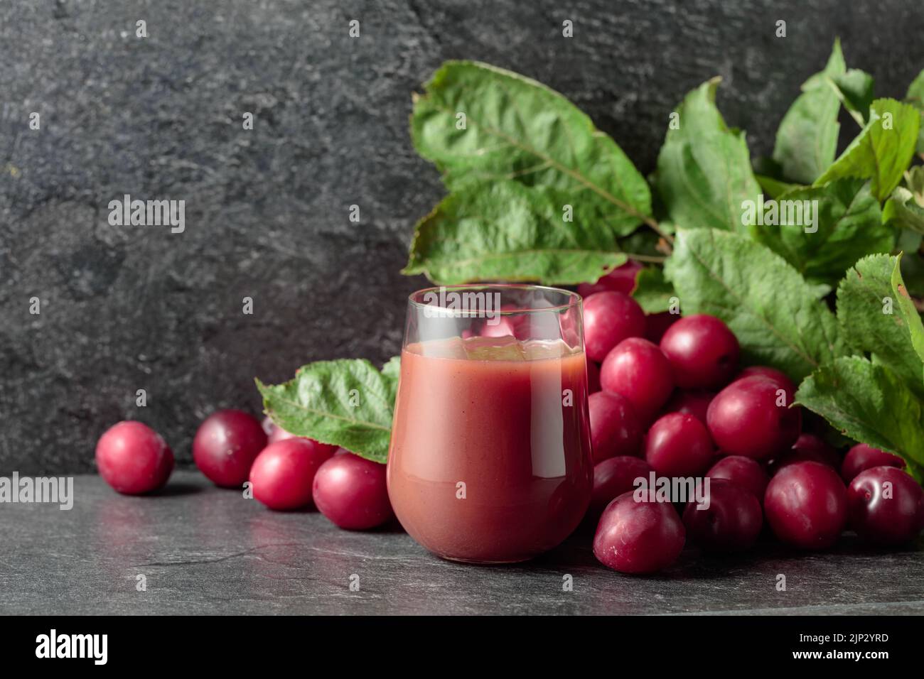 Red plums and a glass of plum juice on a black stone table. Copy space ...