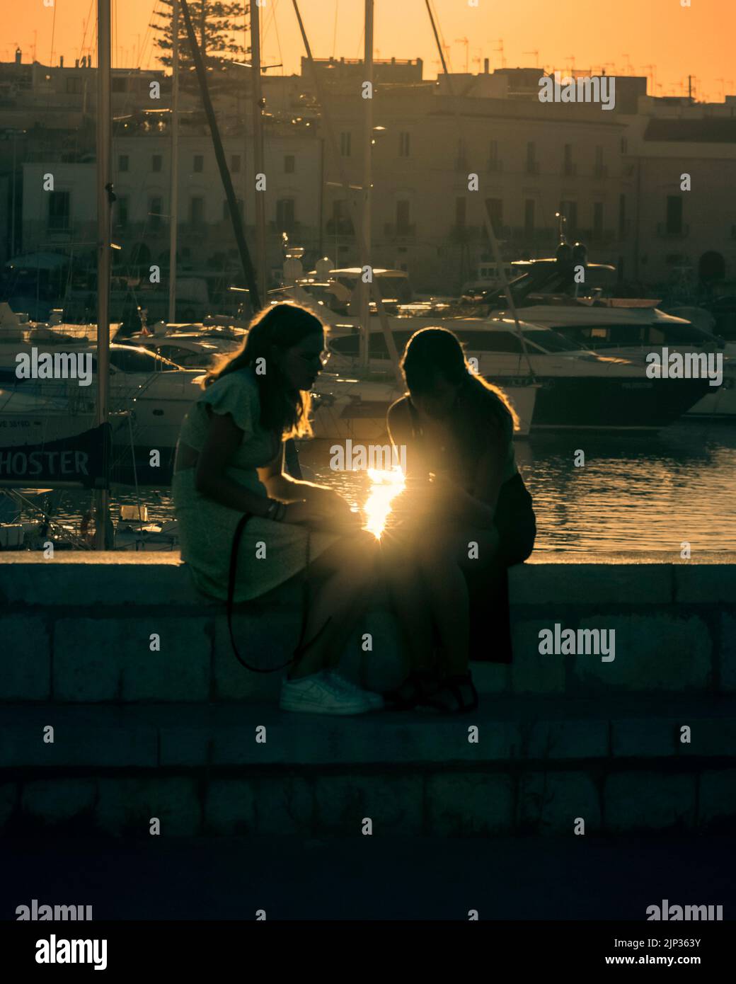 Two girls chat at sunset on the port of Trani, Italy. Trani is a ...
