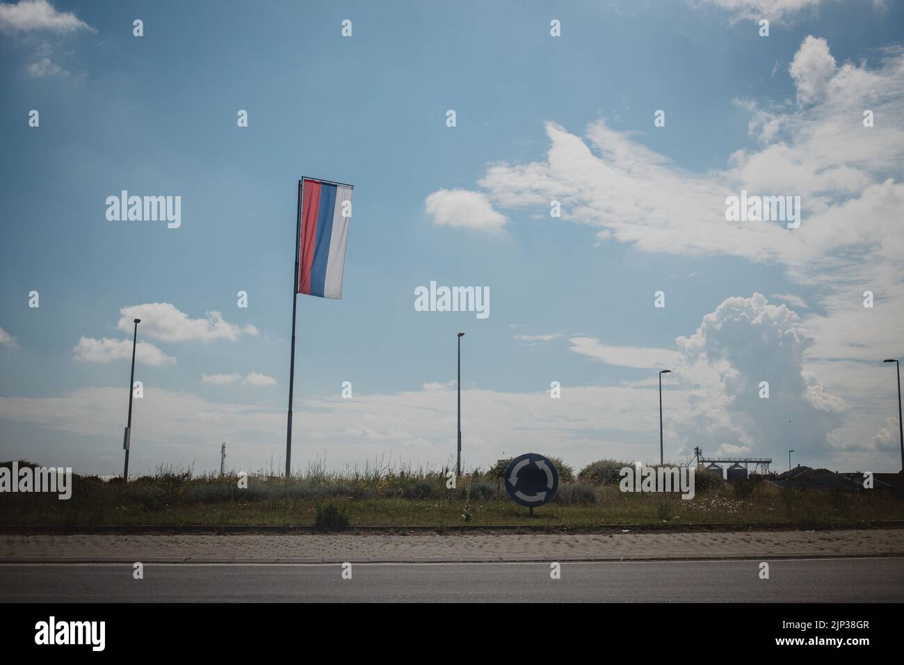 An asphalt road with a flag and forests on the side during daytime ...