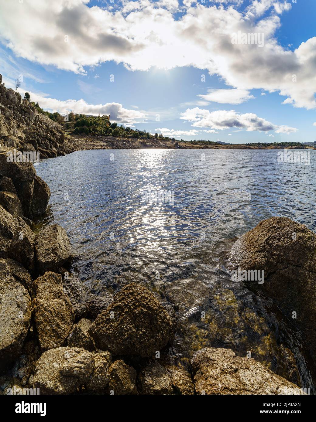 Landscape of rocks in a blue lake with sky with clouds and sun ...