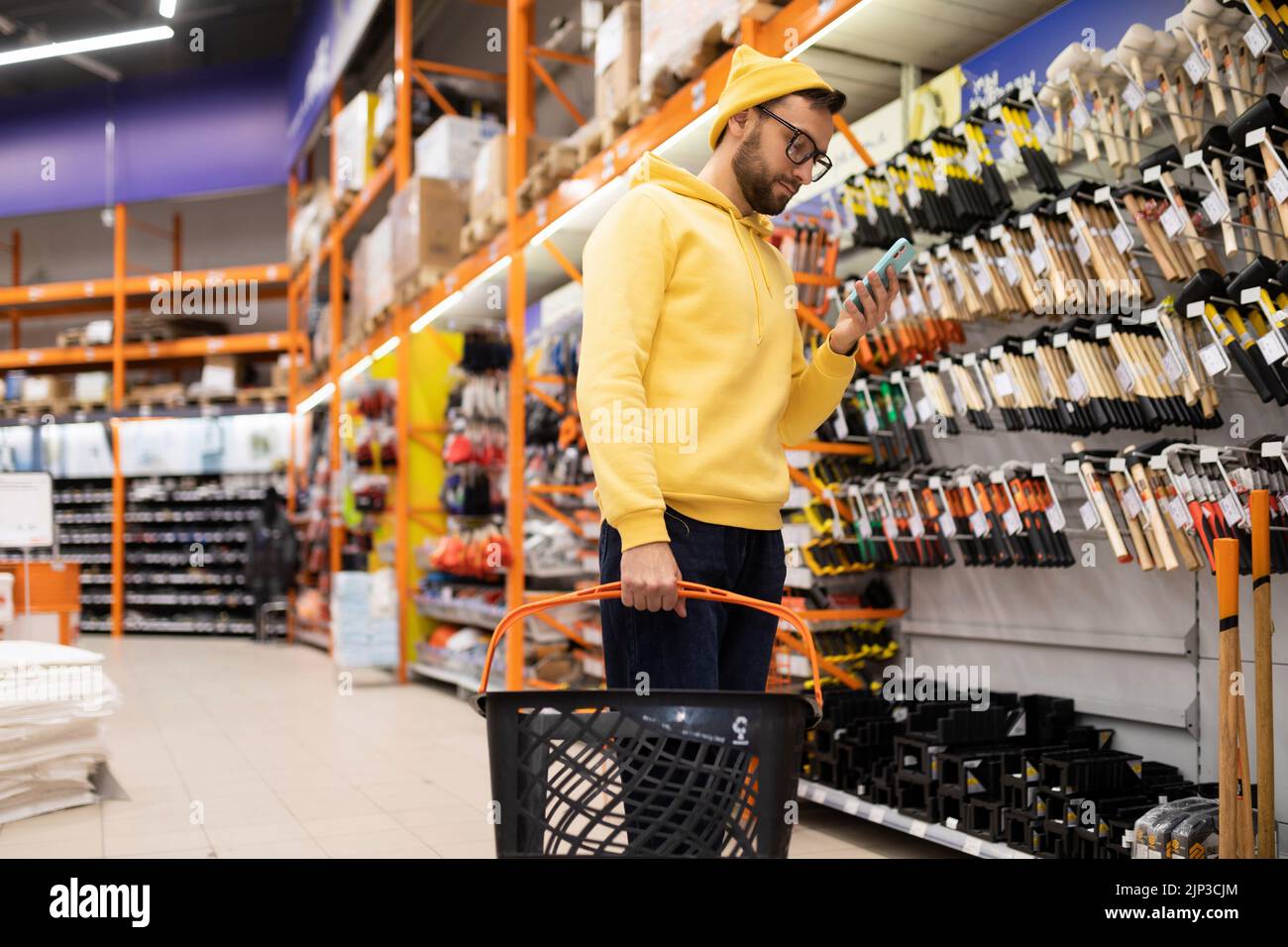a young man in a hardware store next to a rack with hammers and axes ...