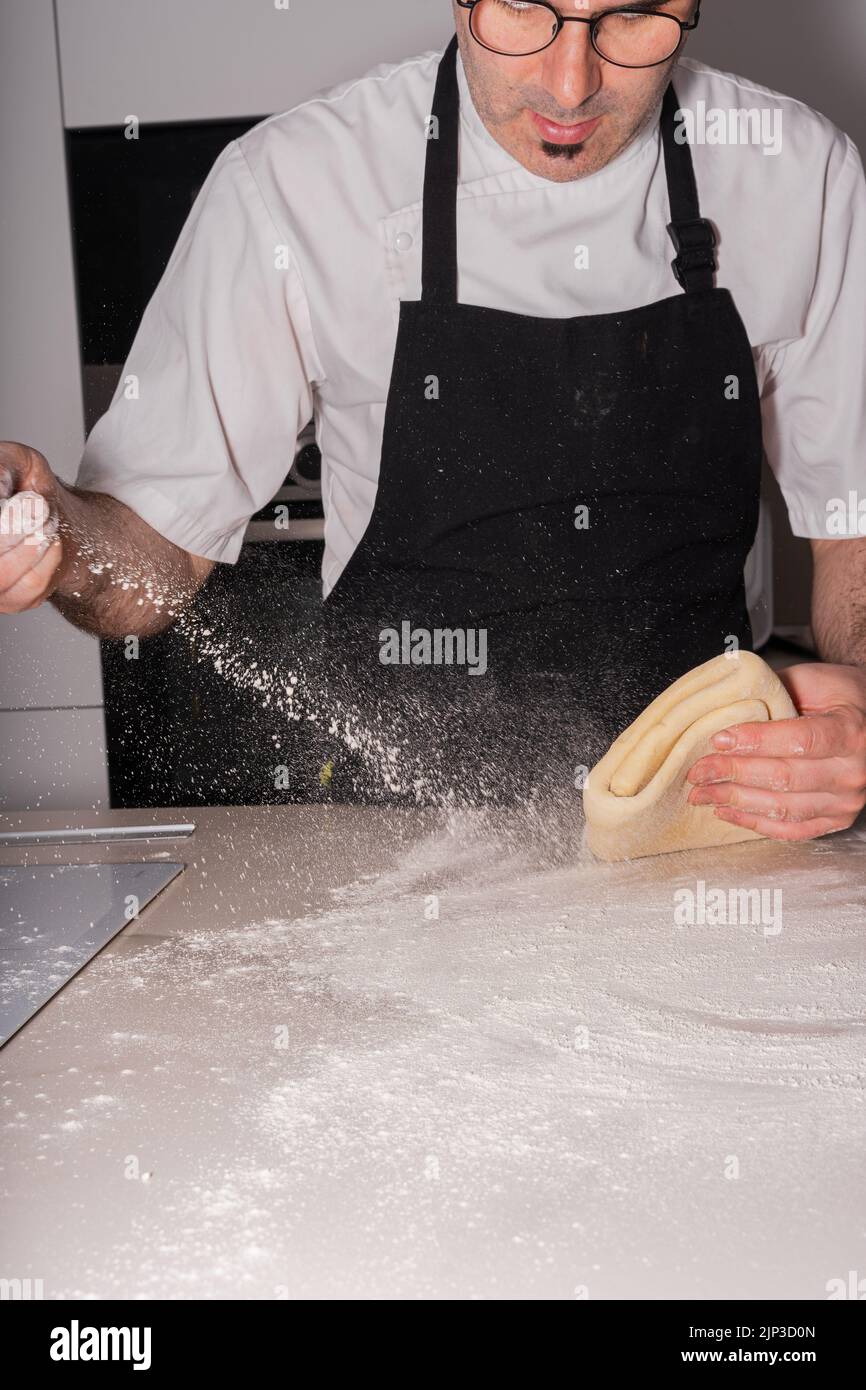 A male confectioner pouring flour on a table to prepare the puff pastry ...