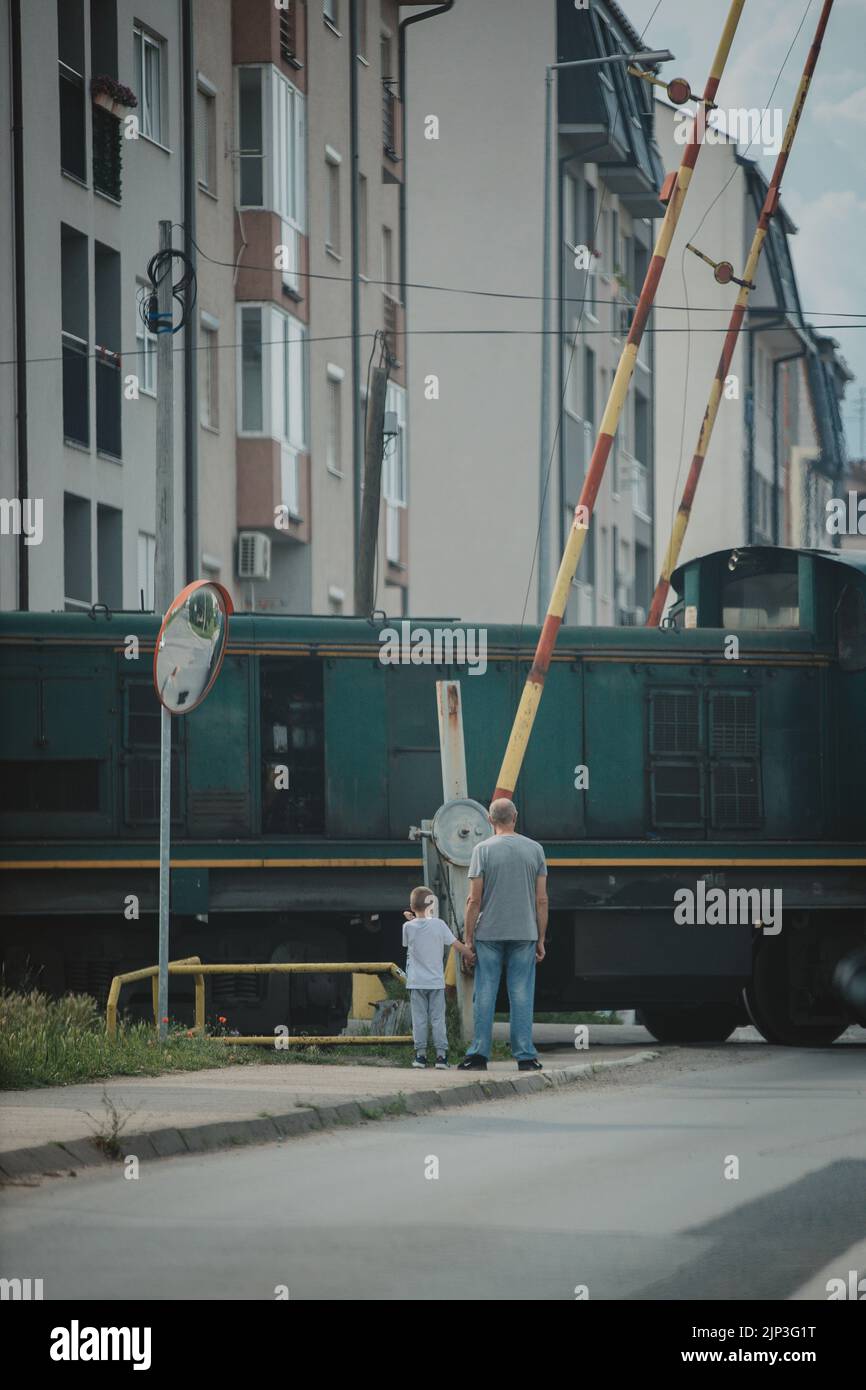 A father and a son from behind in front of a large car and a building ...
