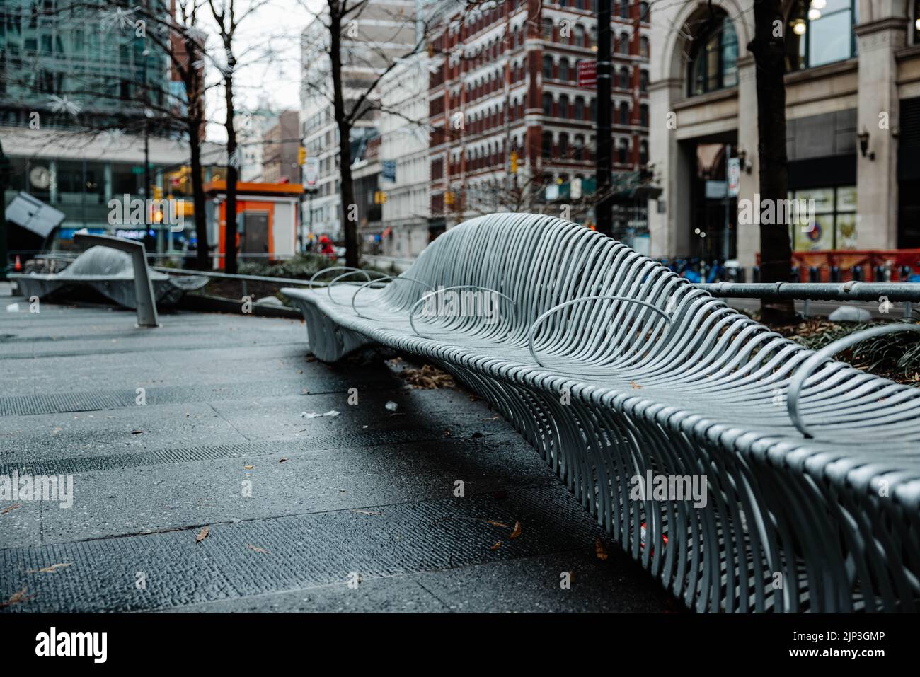 An abstract metal bench on a street with modern buildings in rainy New ...