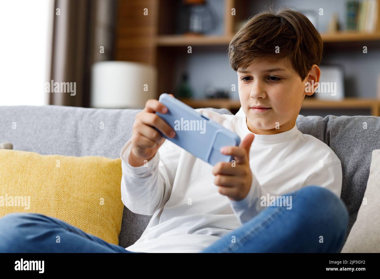 Cheerful young boy playing video game on smartphone sitting on sofa at ...