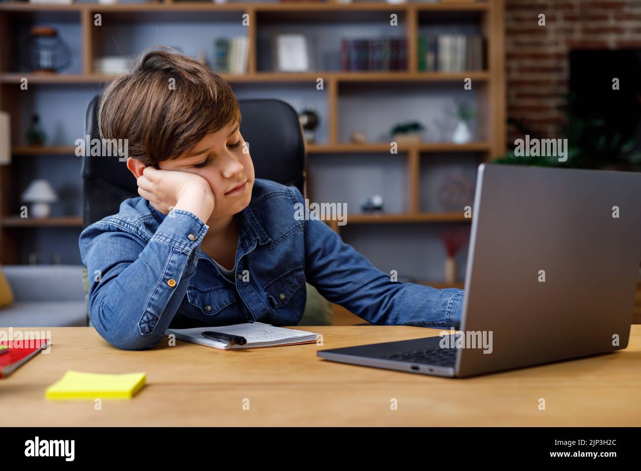 Young boy studying remotely at home using laptop. Tired schoolboy ...