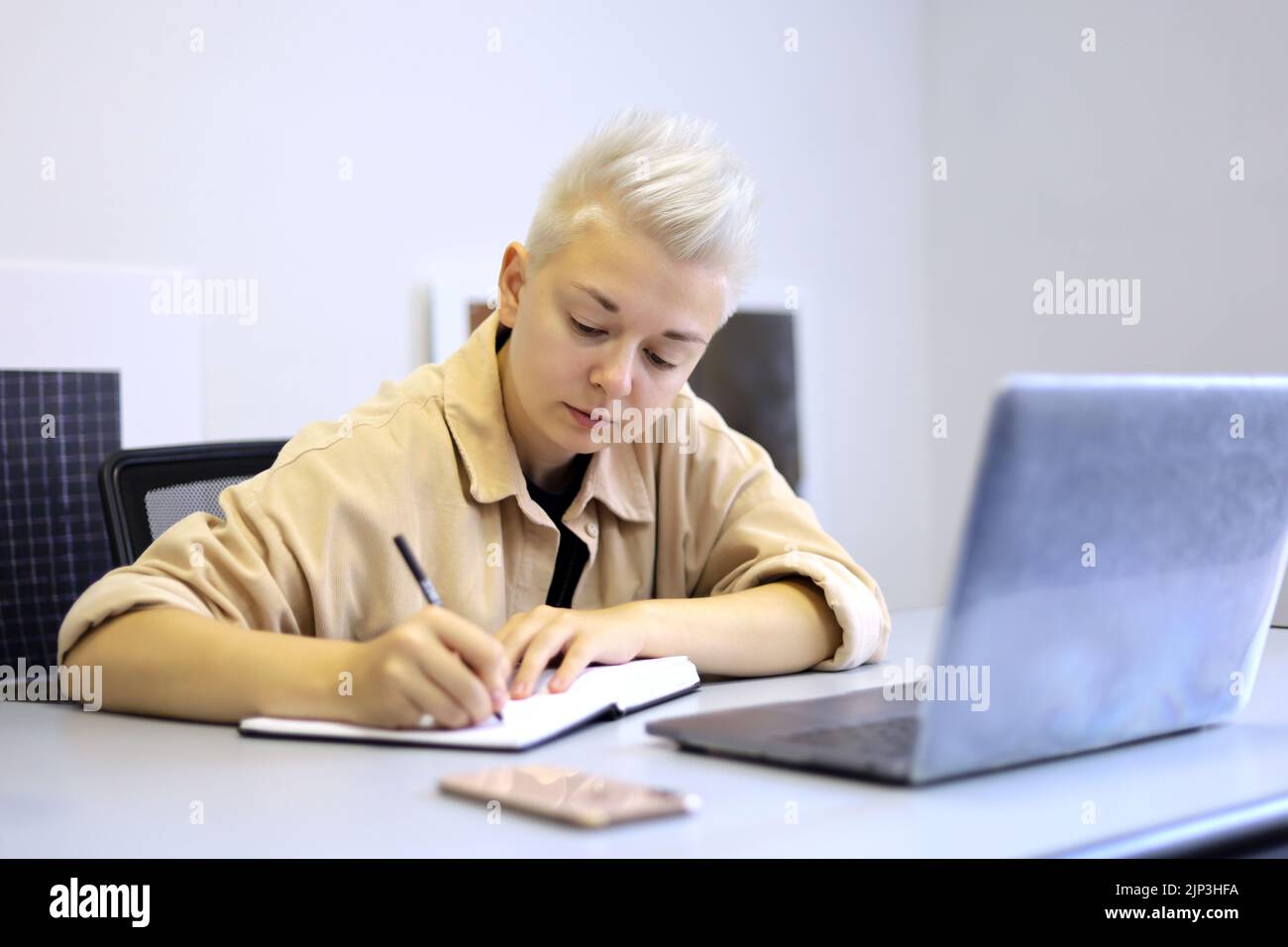 Girl with short blonde hair writes in a notebook while sitting at the ...
