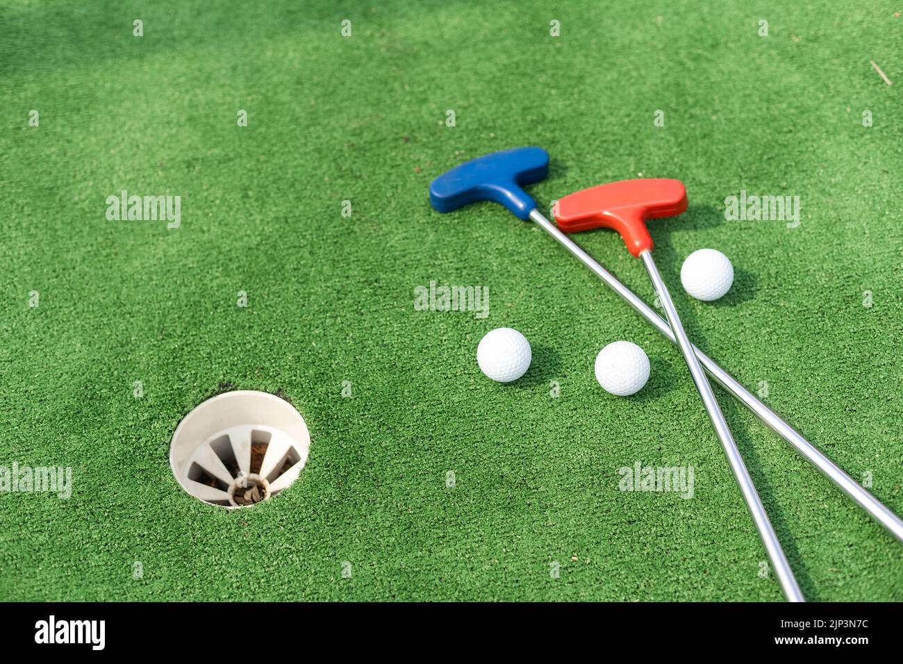 Mini-golf clubs and balls of different colors laid on artificial grass ...