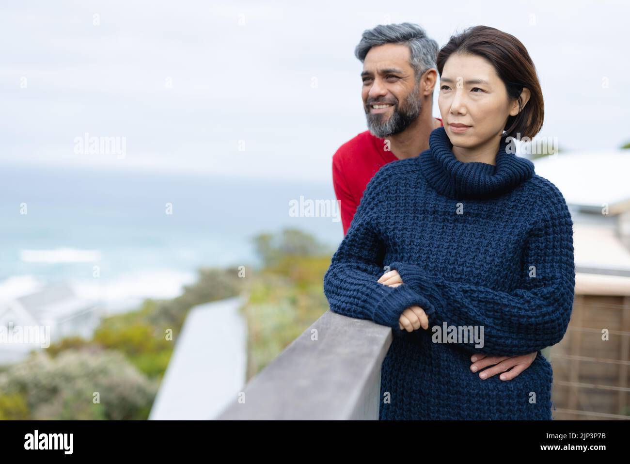 Happy diverse couple embracing and wearing jumpers together at balcony ...