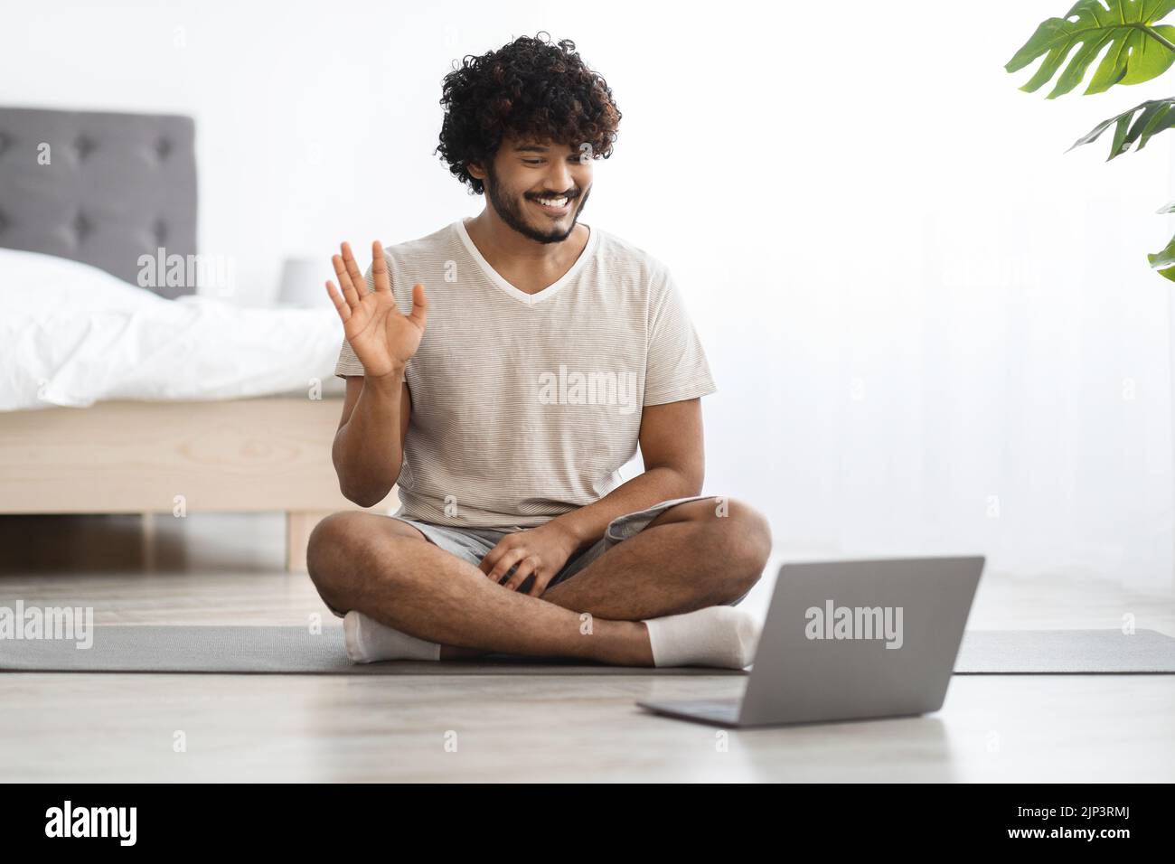 Happy guy sitting on yoga mat, waving at laptop screen Stock Photo - Alamy
