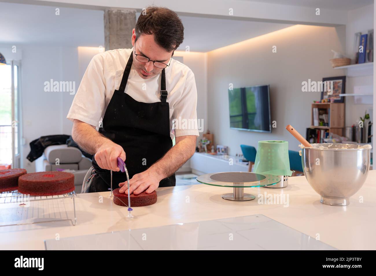 A man baker cooking a red velvet cake at home, cutting the baked cake ...