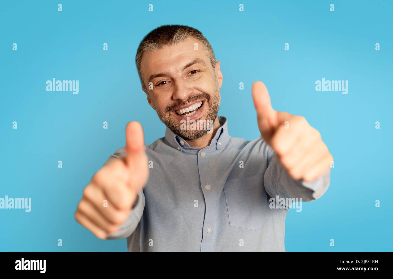 Joyful Male Gesturing Thumbs Up With Both Hands, Blue Background Stock ...