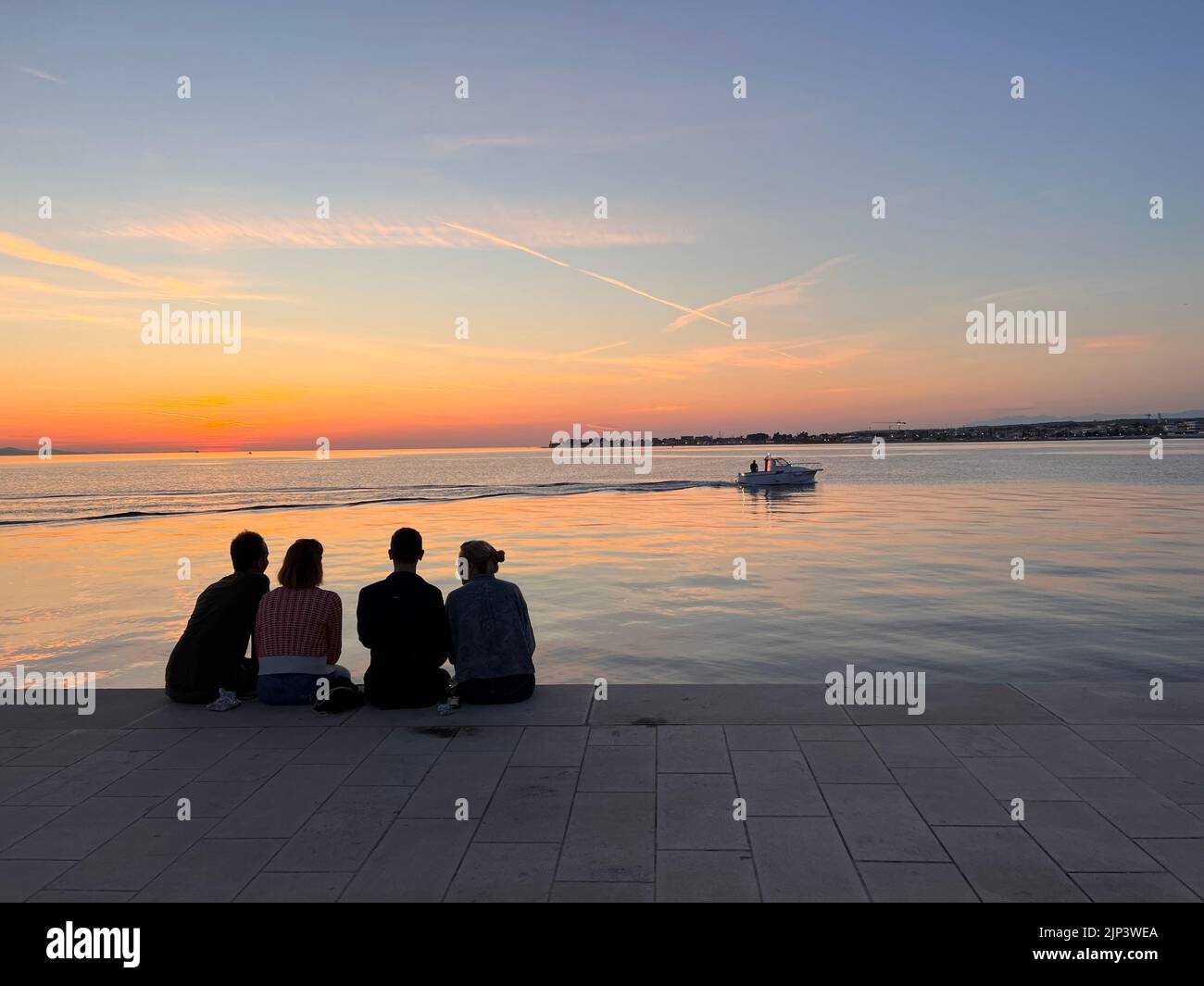 People sitting at a shore and watching a beautiful sunset in Zadar ...