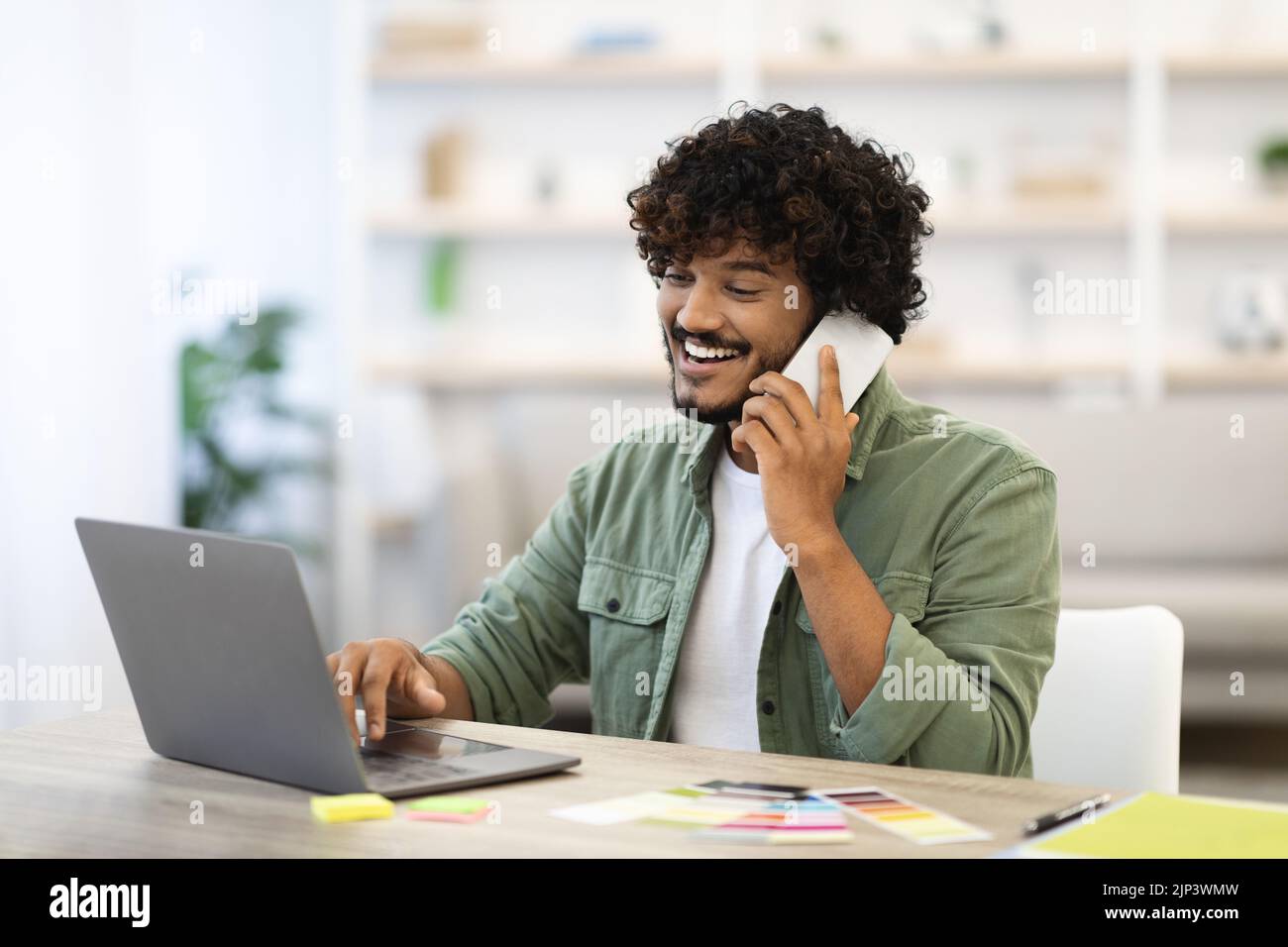 Cheerful indian guy entrepreneur working online, having phone ...