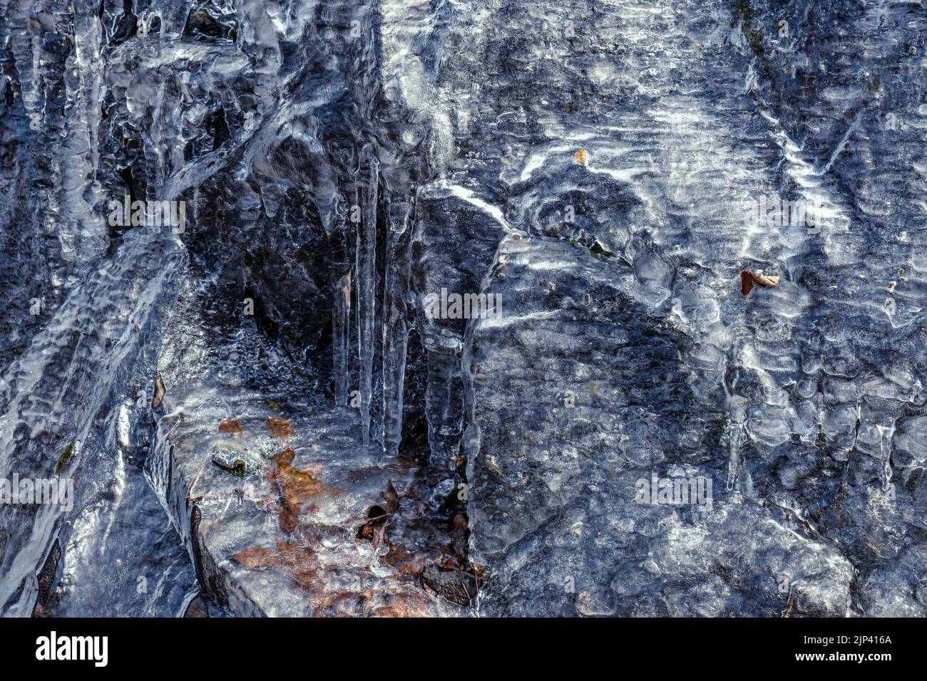 Narrow streams of water run under a thin sheet of ice and over stone ...