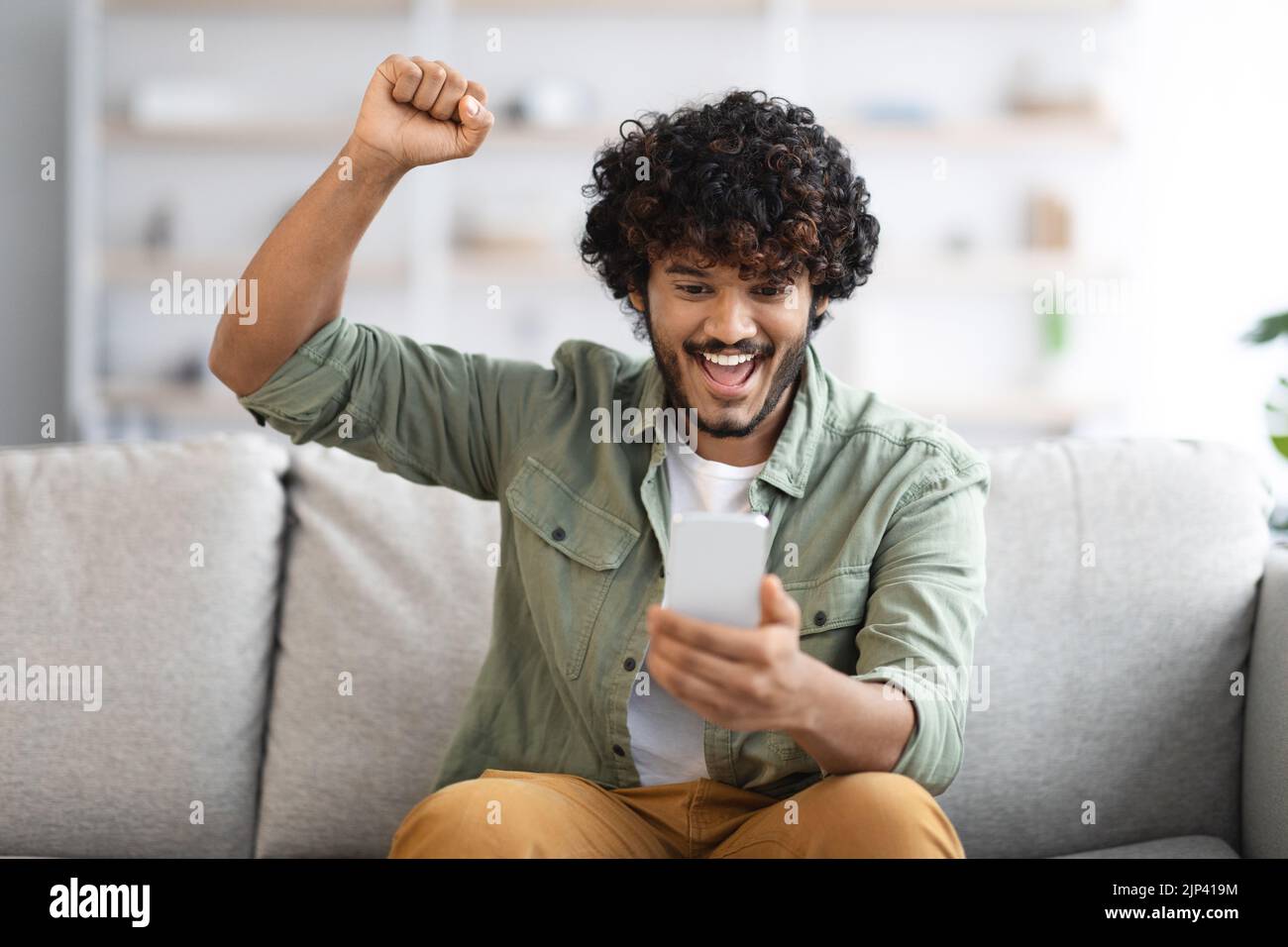 Emotional indian guy holding cell phone, raising hand up Stock Photo ...