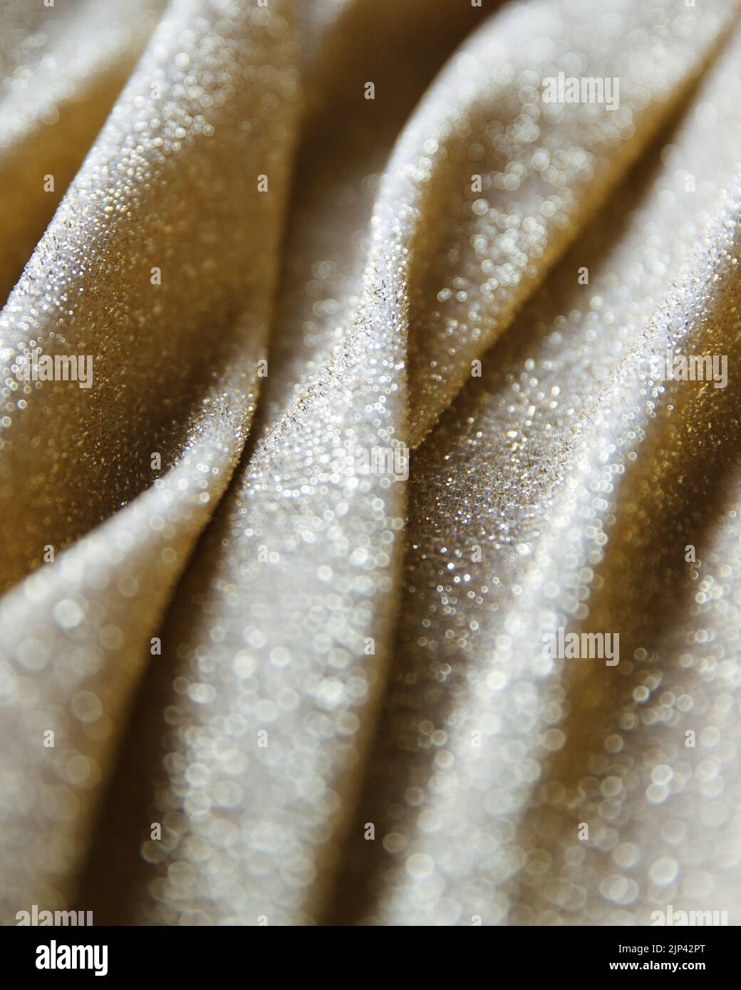 A vertical closeup of a golden textile flowing material with lots of ...