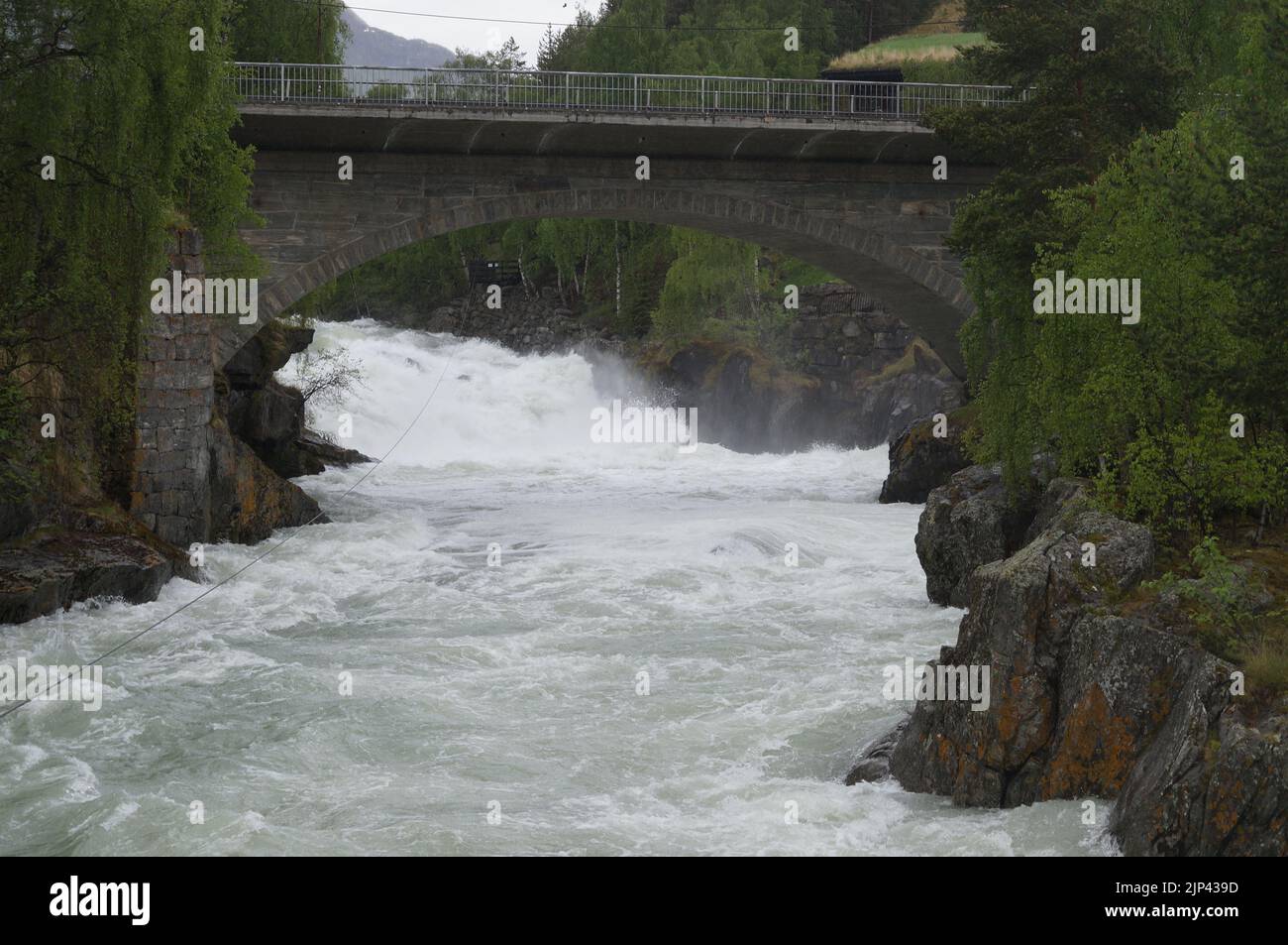 An arch bridge over a river surrounded with big rocks and trees in Oslo ...