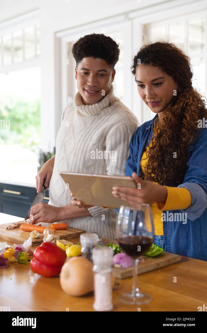 Happy Biracial Couple Preparing Food Using Recipe On Tablet In Kitchen