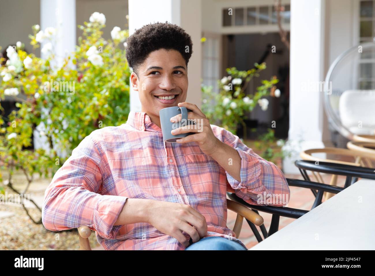 Happy biracial man sitting on garden terrace drinking coffee outside ...
