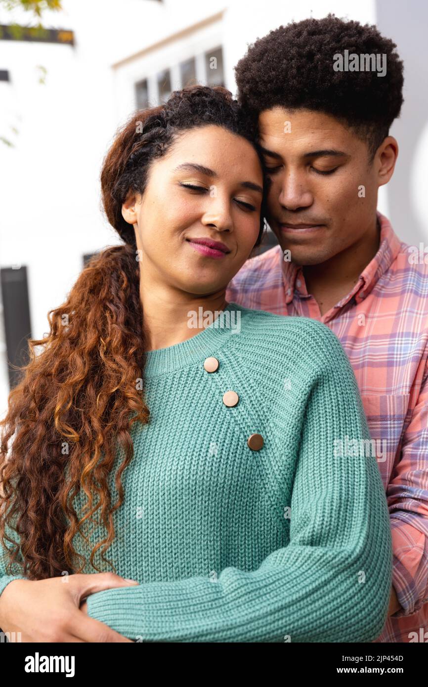 Happy biracial couple embracing with eyes closed on terrace outside ...