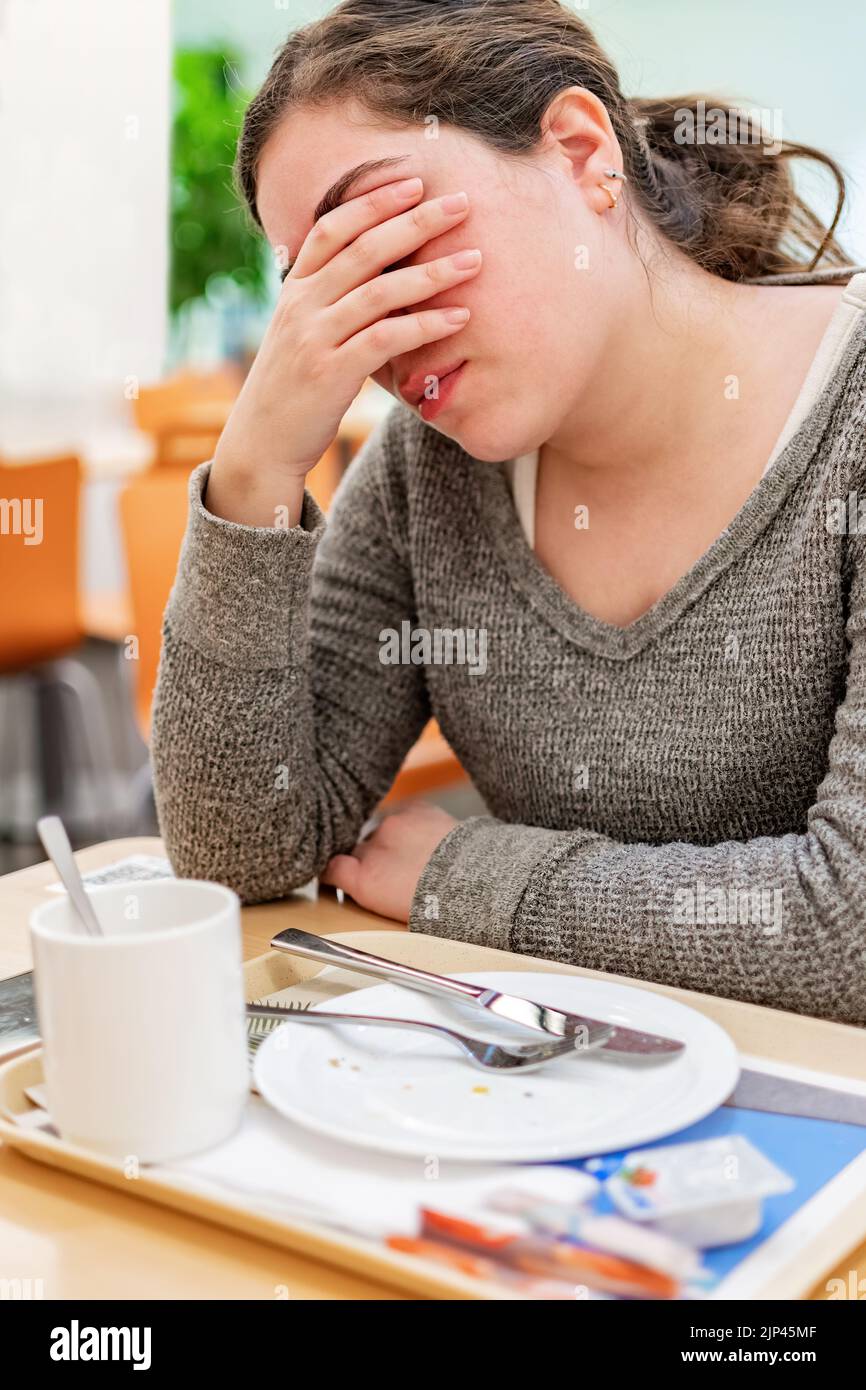 A young tired Caucasian woman taking breakfast at morning covering her ...