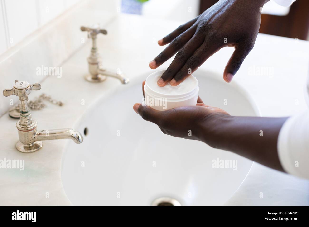 Hands of african american man using moisturiser face cream at sink in ...