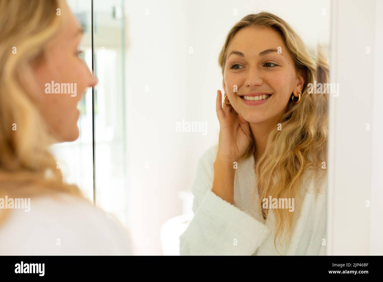 Happy caucasian woman wearing robe, looking at her reflection in mirror ...