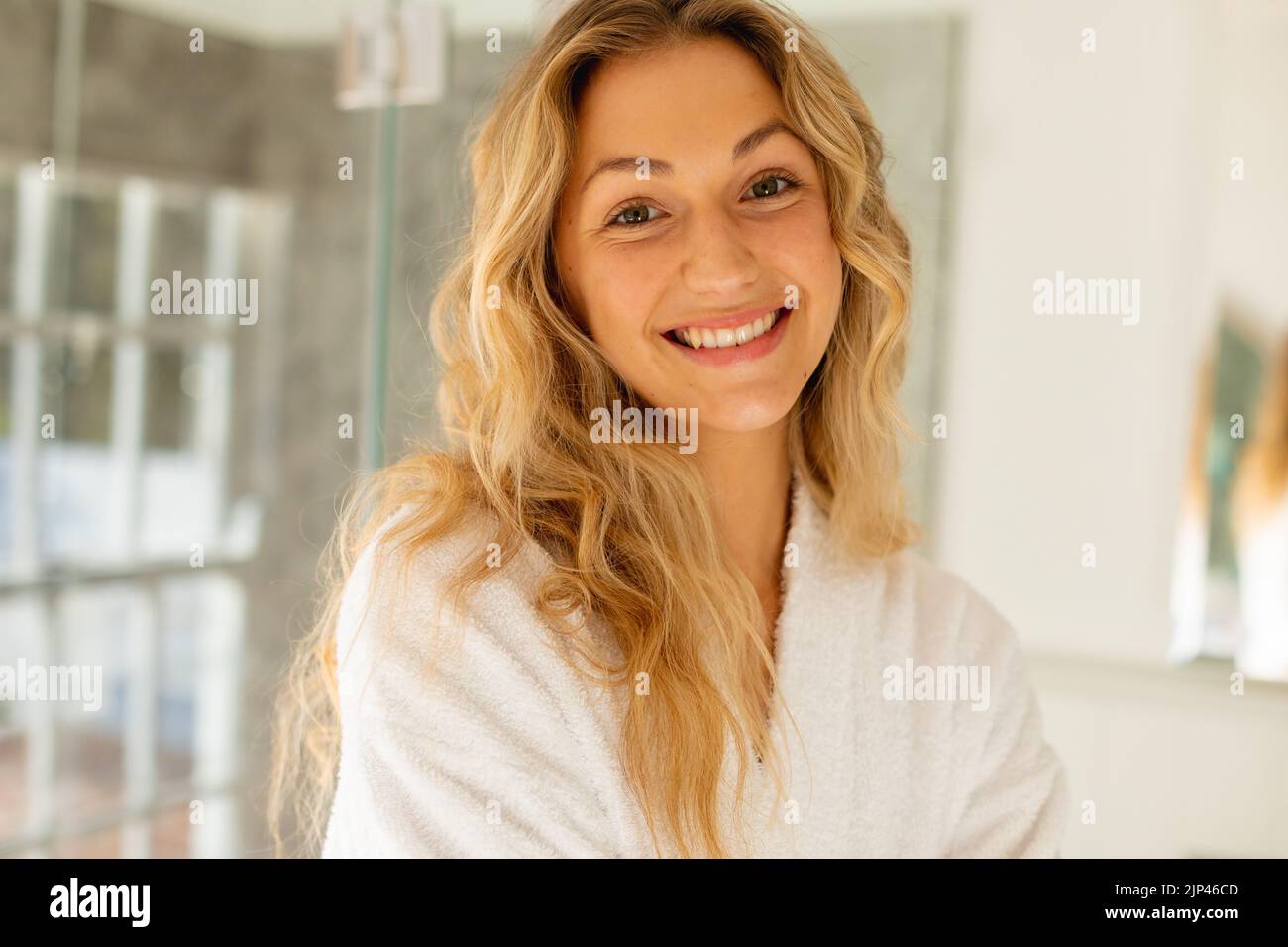 Portrait of happy caucasian woman wearing robe, smiling in bathroom ...