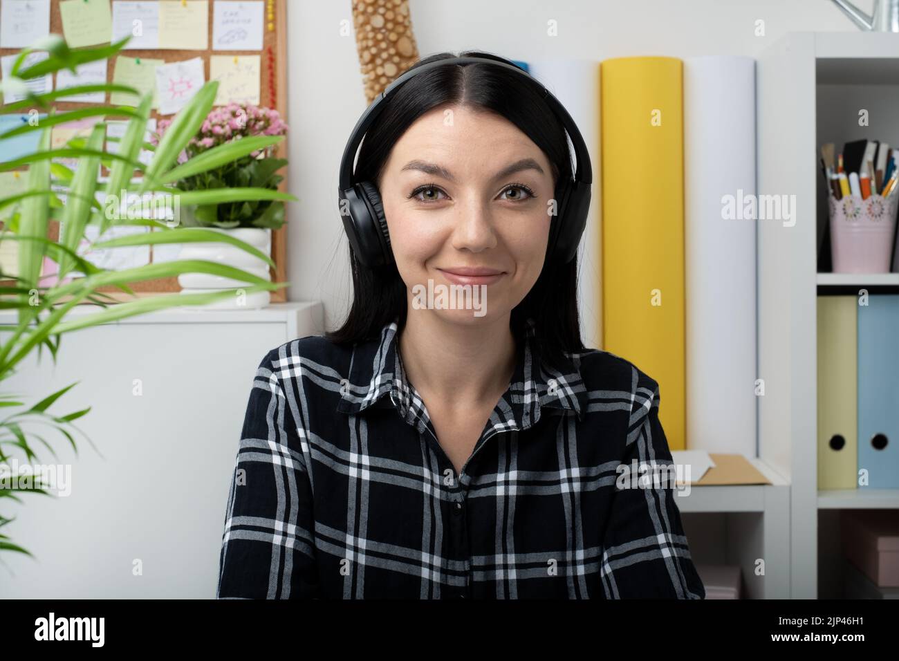 Happy smiling young female wearing wireless headphones is looking at the camera. Online working ...