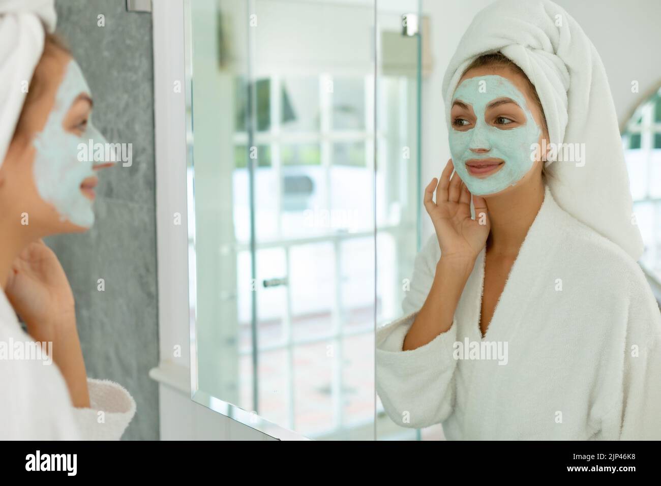 Happy caucasian woman wearing robe, applying beauty face mask on face ...