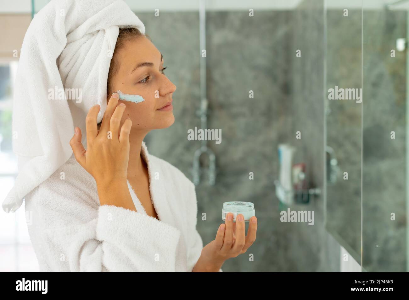Happy caucasian woman wearing robe, applying beauty face mask on face ...