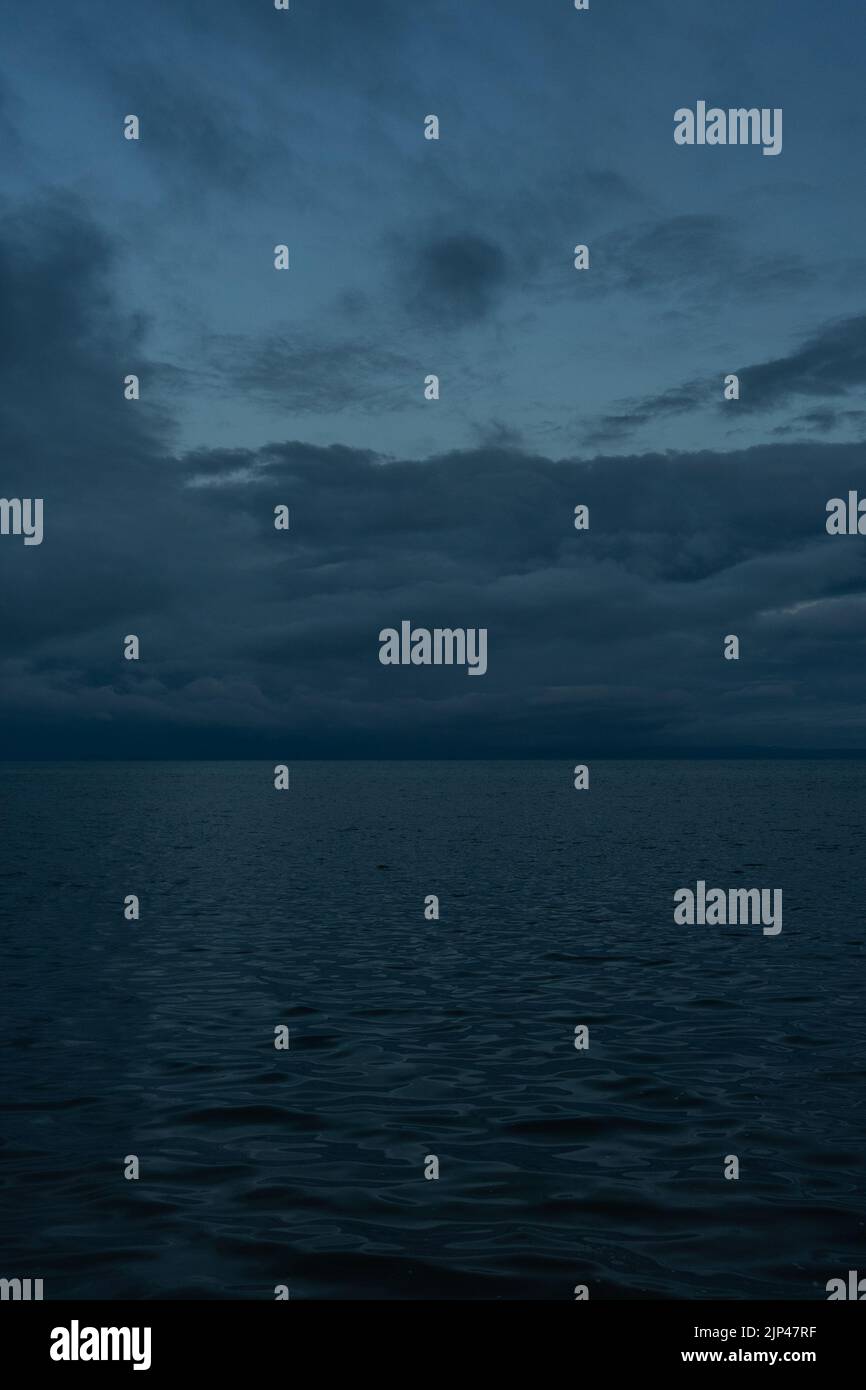 A vertical view of the evening lake with calm water and gray gloomy ...